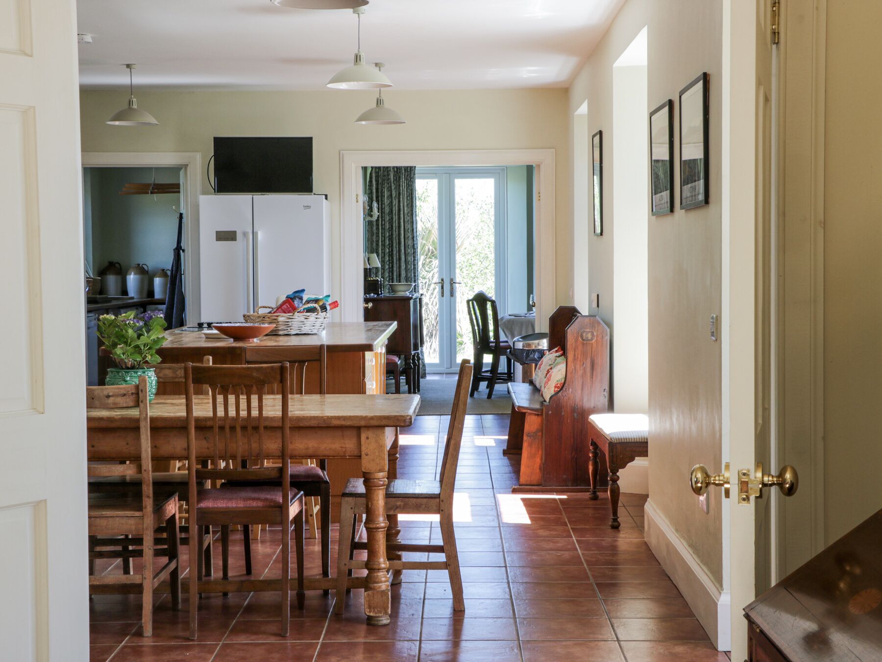 Cozinha com mobiliário de madeira, mesa de jantar e cadeiras. Há uma geladeira, pia e janela com cortinas.