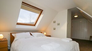 Quarto com uma cama grande, um claraboia, cabeceira de madeira, abajures e uma porta.