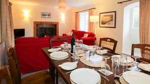 Uma sala de jantar com uma mesa de madeira posta para quatro pessoas, um sofá vermelho e uma lareira.