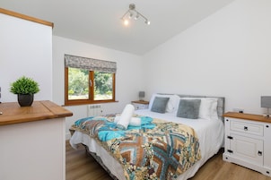 Quarto com cama, mesas de cabeceira, radiador, janela com vista e luminária no teto.