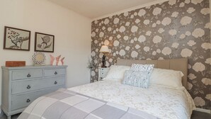Quarto com cama, cômoda e papel de parede floral.