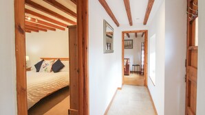 Um corredor estreito com vigas de madeira e uma cama com almofadas no quarto à esquerda.