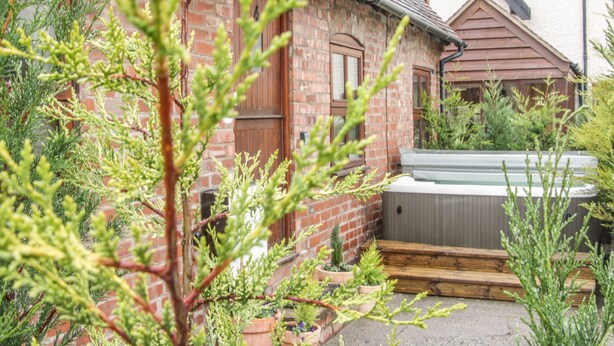 Uma casa de tijolos com porta de madeira, uma banheira de hidromassagem e plantas em vasos.