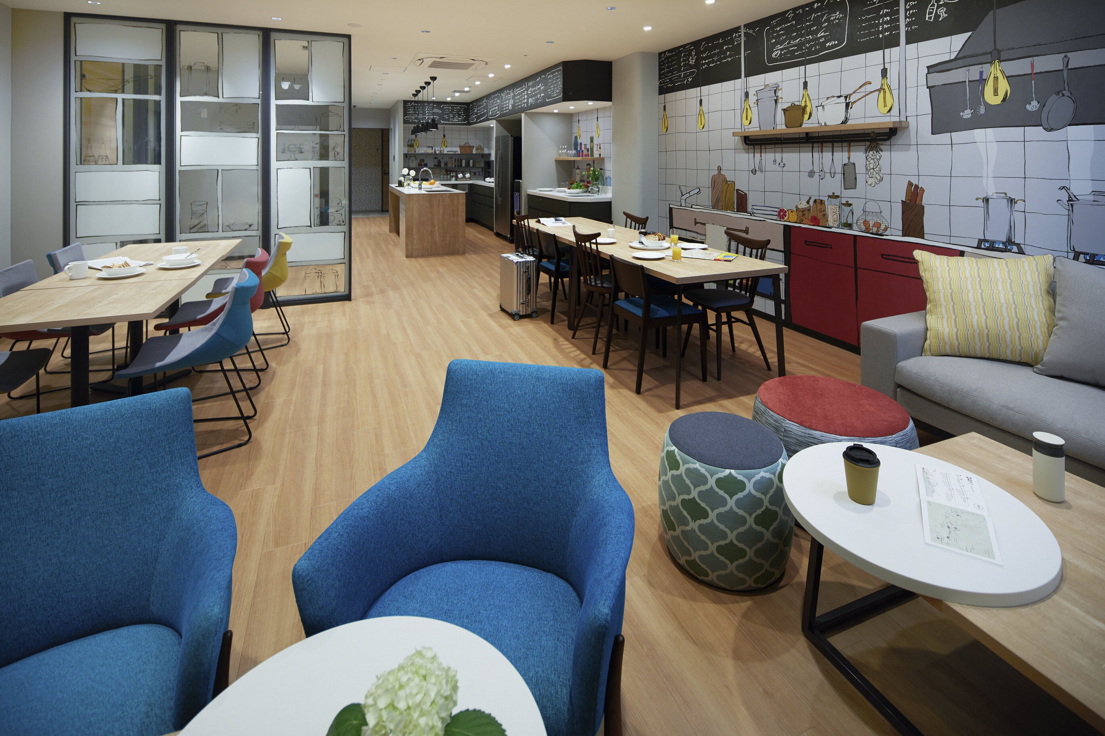 Uma área de jantar moderna com uma mesa grande, cadeiras azuis e uma cozinha ao fundo.