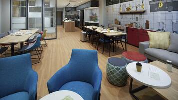Uma área de jantar moderna com uma mesa grande, cadeiras azuis e uma cozinha ao fundo.