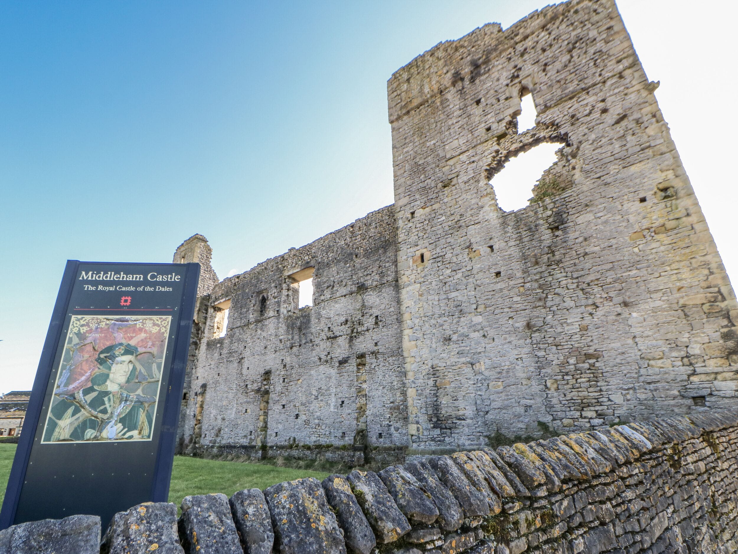 Ruínas do Castelo de Middleham com uma placa de identificação.