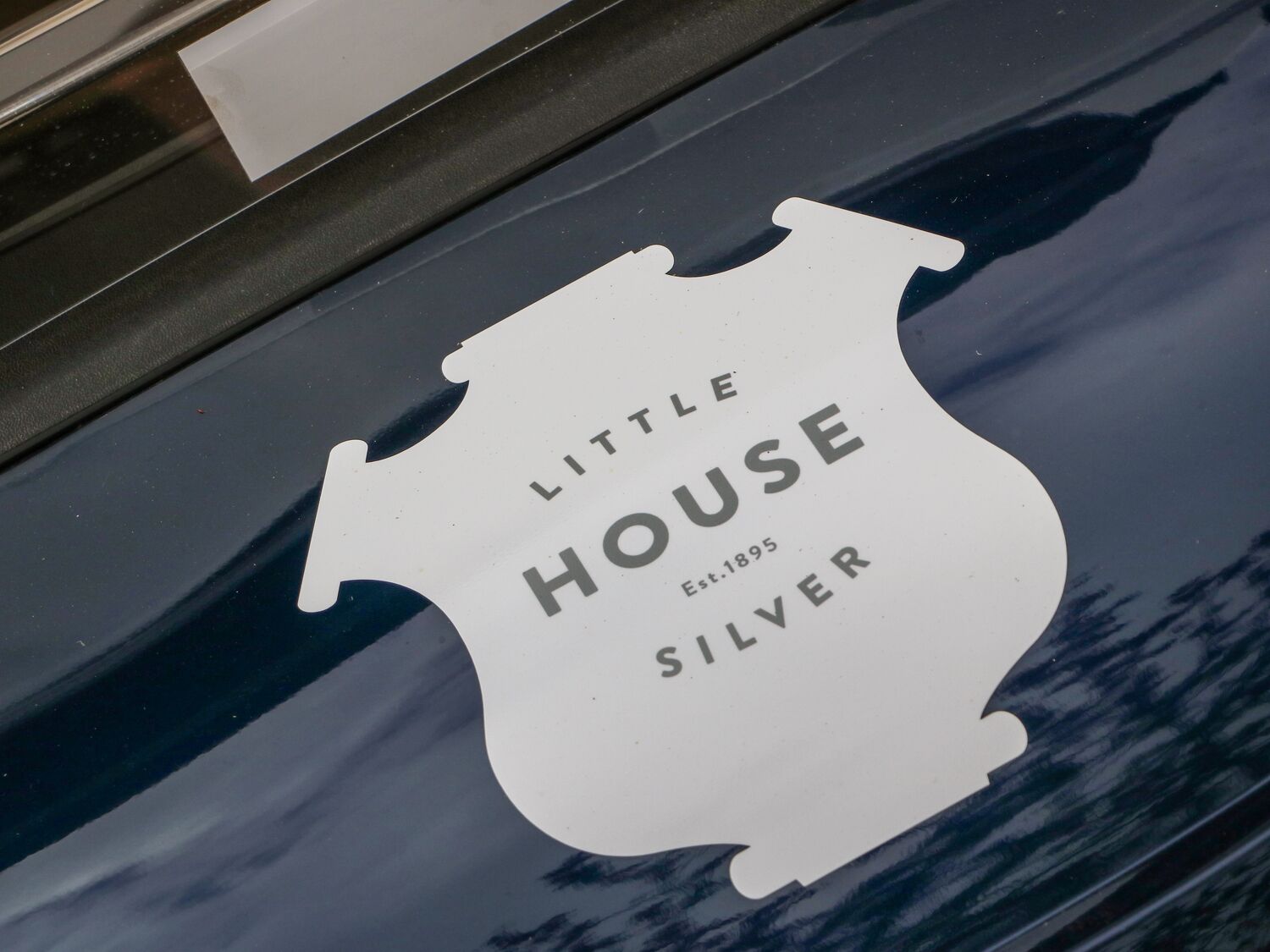 Um autocolante no para-brisas do carro com o texto 'Little House Silver' e 'Fundada em 1895'.