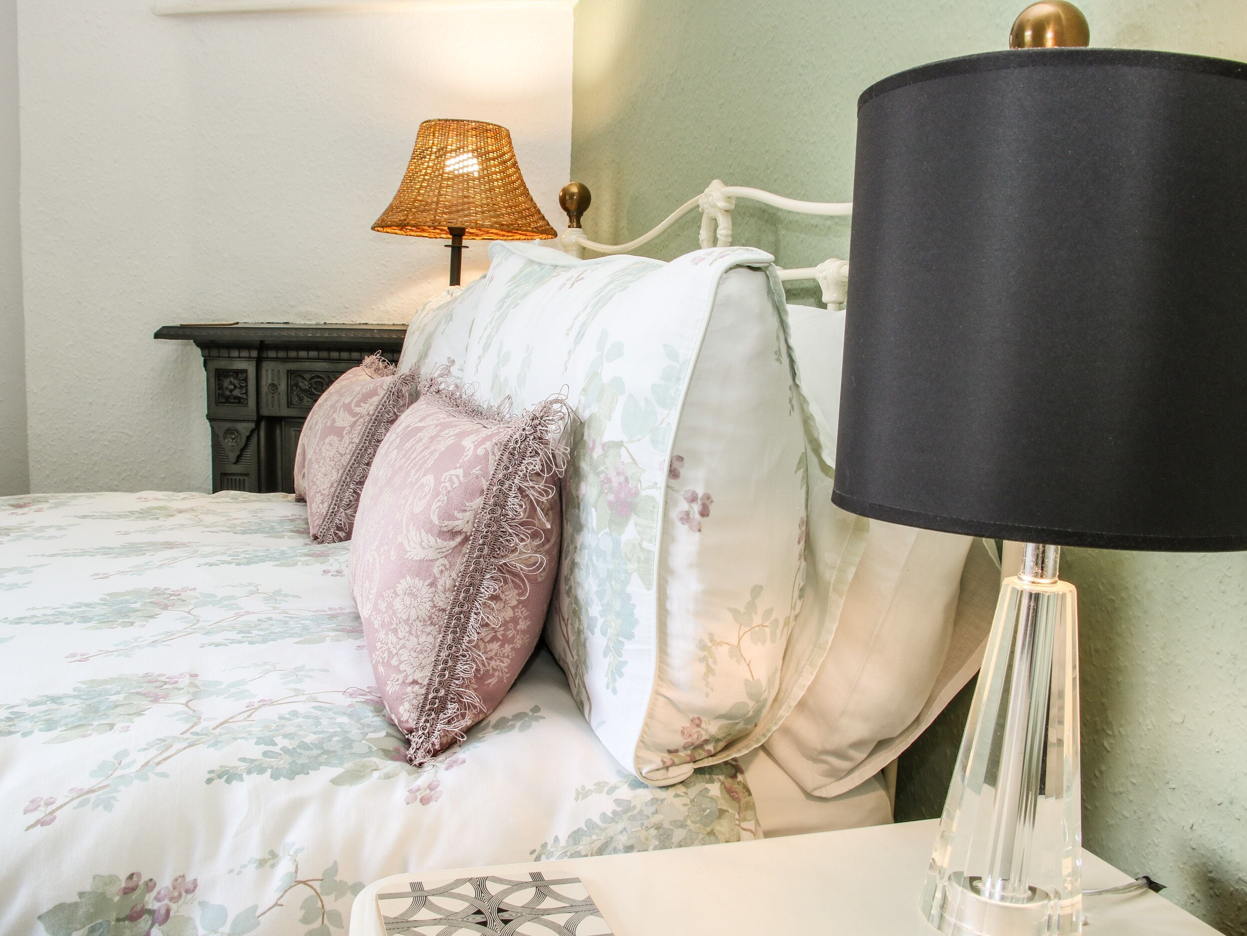 Cama bem arrumada com roupa de cama florida, luminária preta e mesa de cabeceira em estilo vintage com luminária.