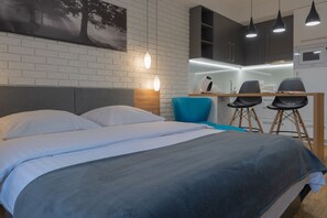 Quarto de hotel moderno com uma cama, uma escrivaninha com duas cadeiras, um micro-ondas e uma janela grande.