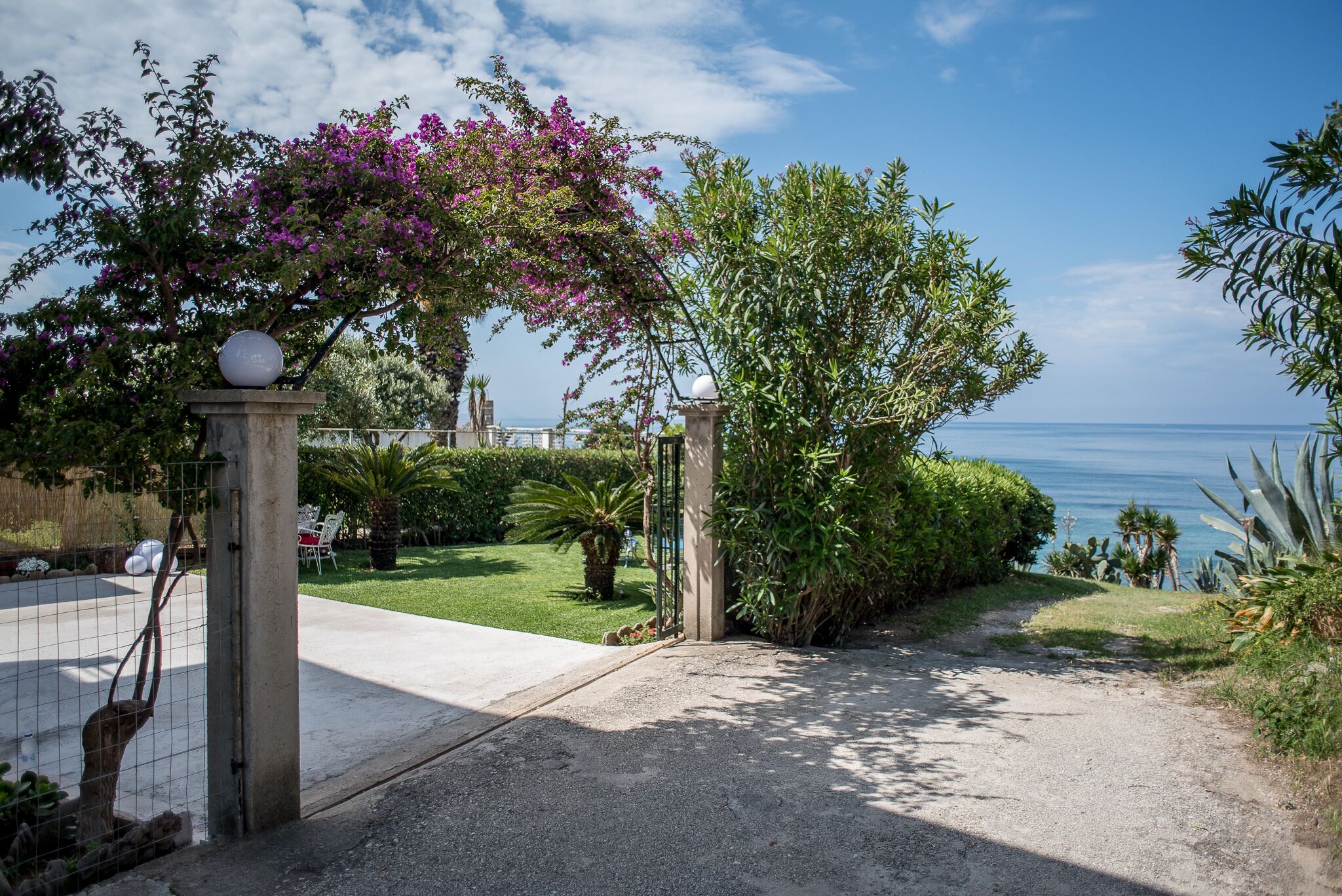 Um caminho pavimentado leva a um portão com um arco decorativo e vista para o mar.