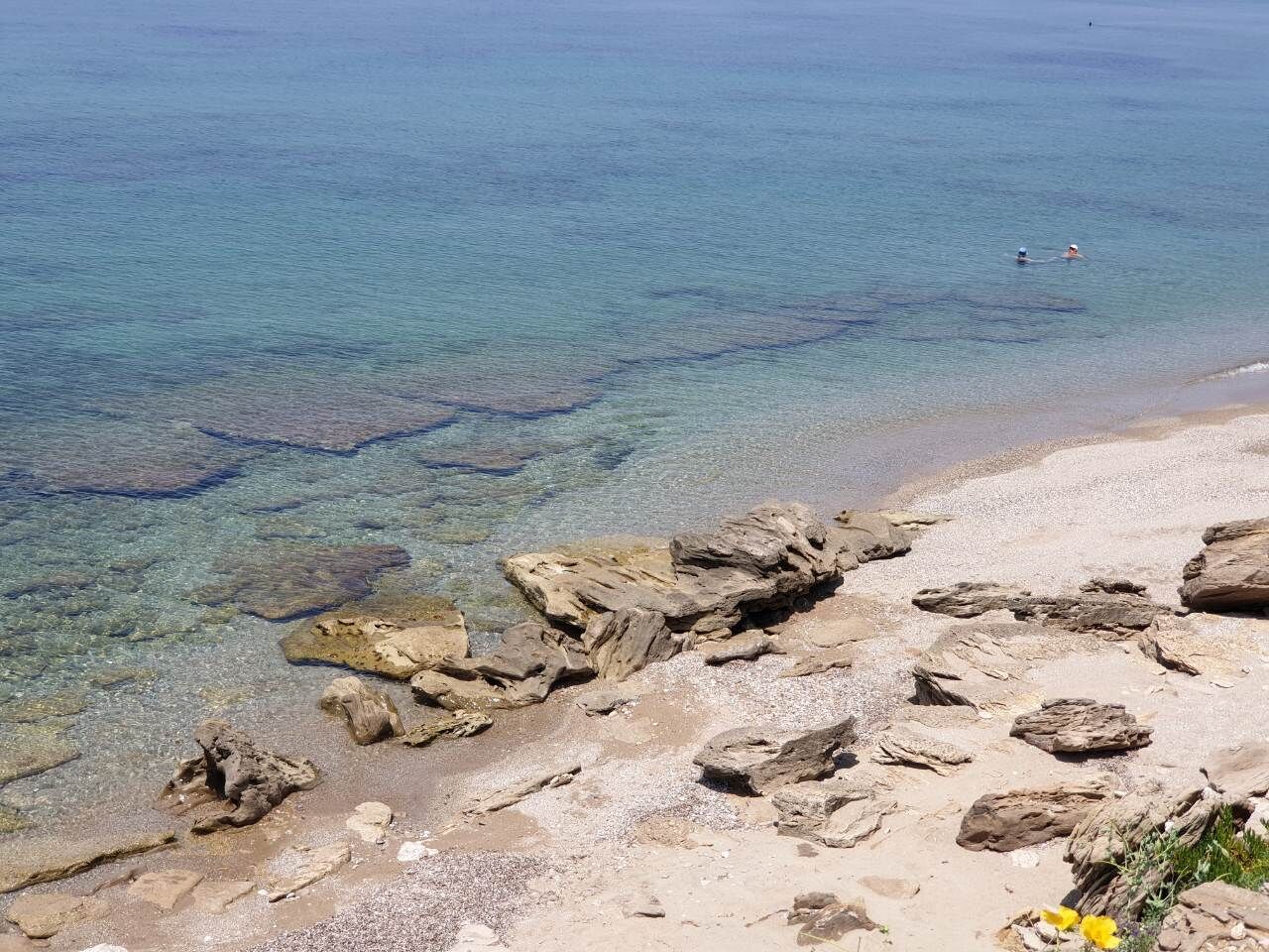 Uma praia rochosa com águas cristalinas e algumas pessoas ao longe.