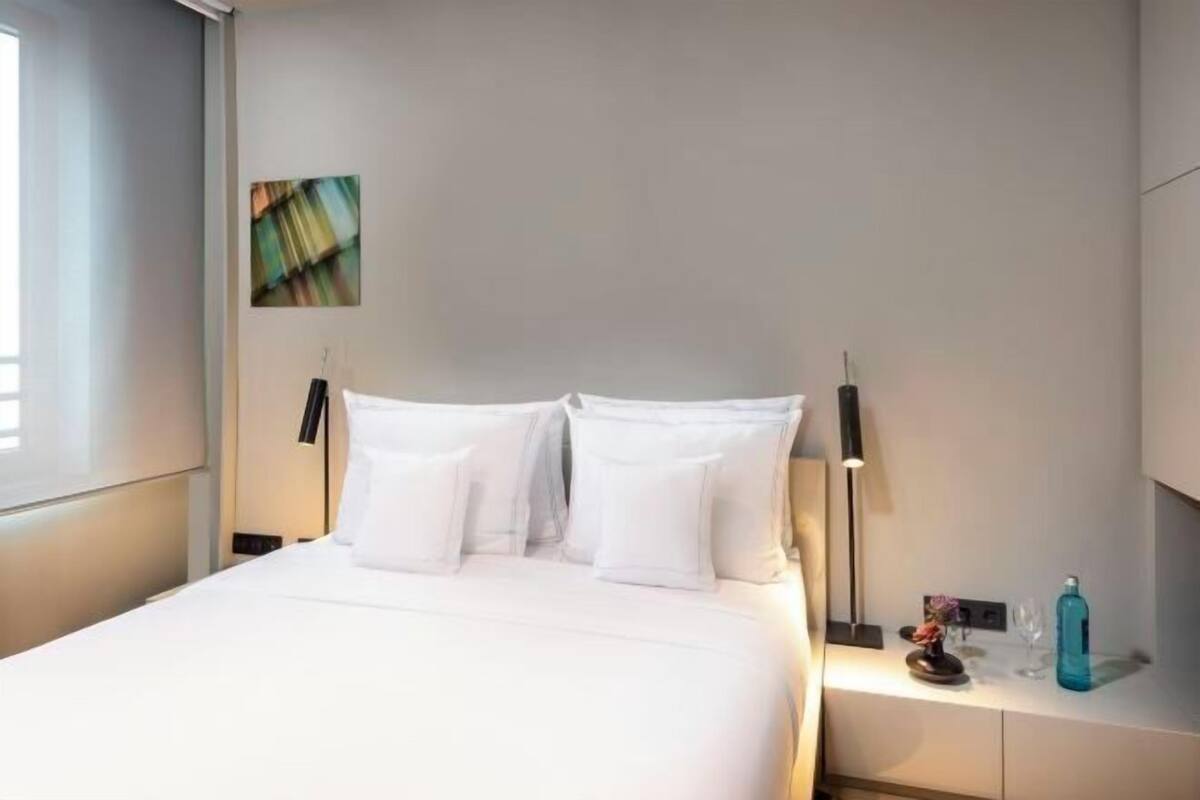 Quarto de hotel com uma cama, mesas de cabeceira, luminária e uma obra de arte na parede.