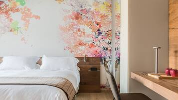 Quarto com cama, mesa de cabeceira de madeira, escrivaninha com cadeira e um mural floral colorido na parede.