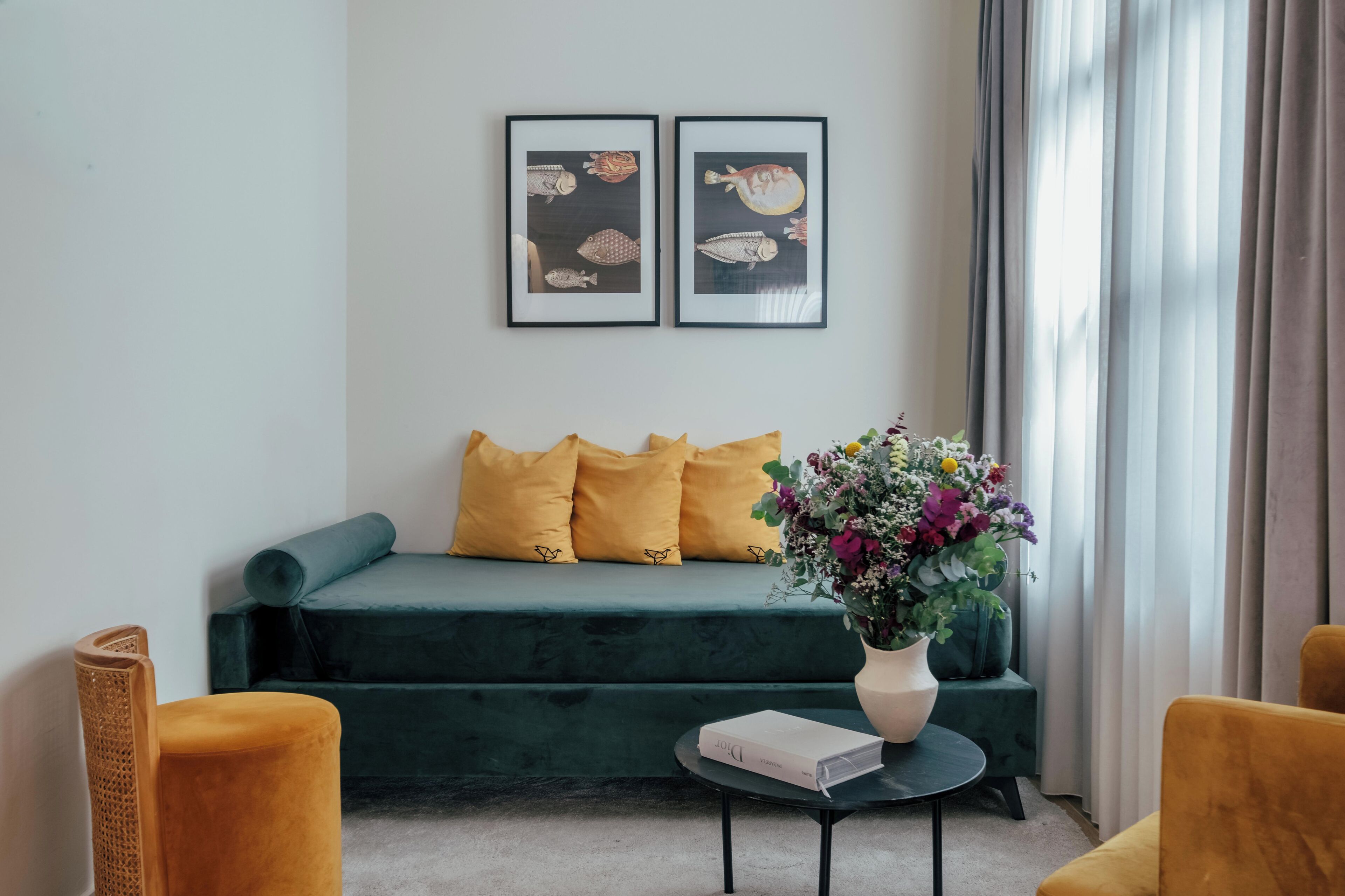 Uma sala de estar moderna com um sofá verde, almofadas amarelas, uma mesa redonda com um livro e um vaso de flores.