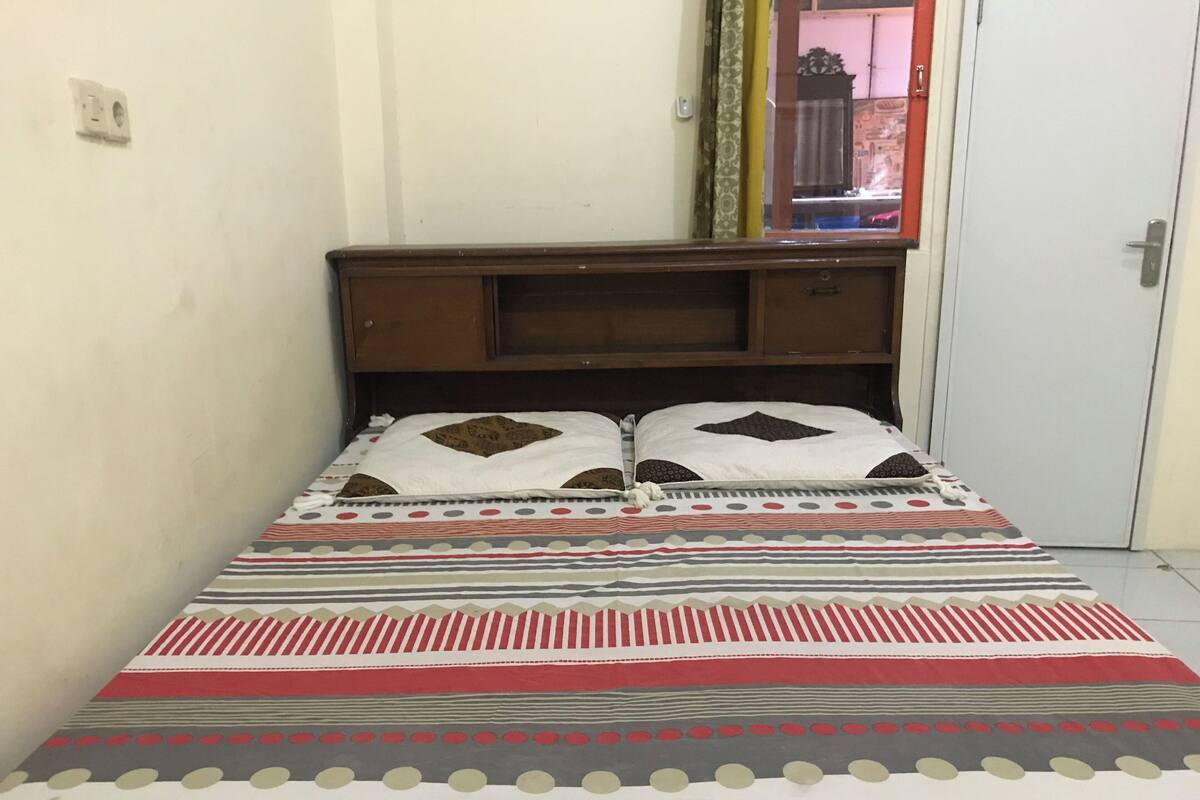 Uma cama com colcha estampada, cabeceira de madeira e um espelho na parede.