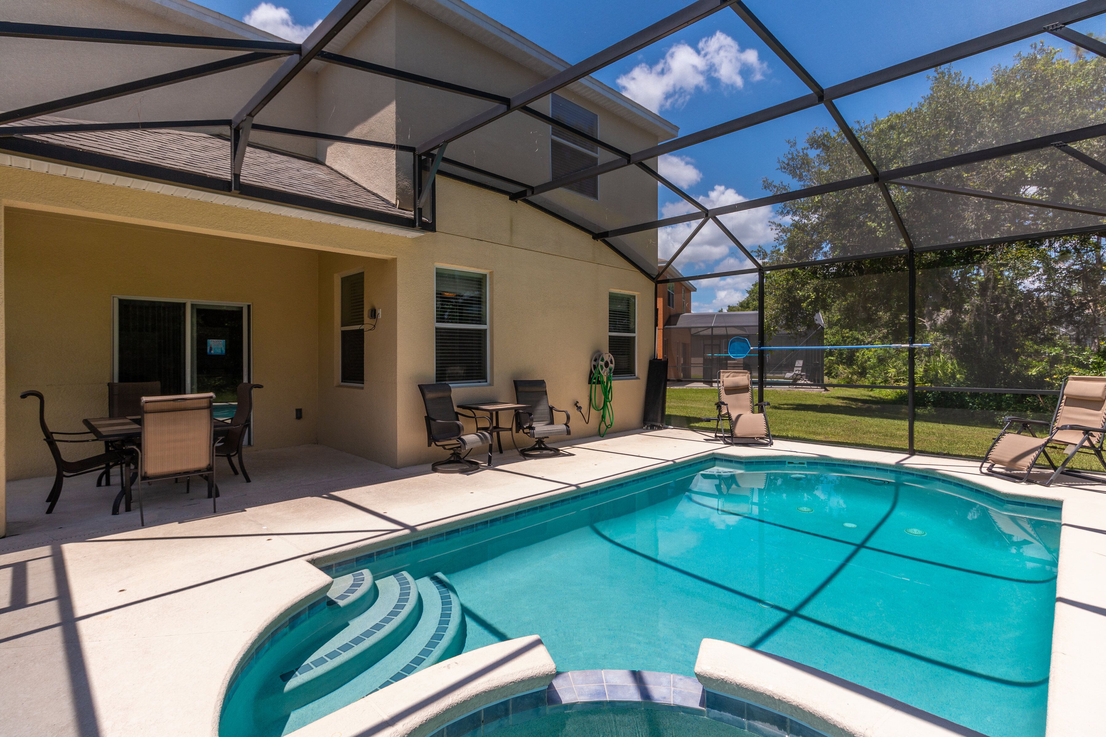 Piscina com toldo de sol, área de estar ao ar livre e vista para o verde ao redor.