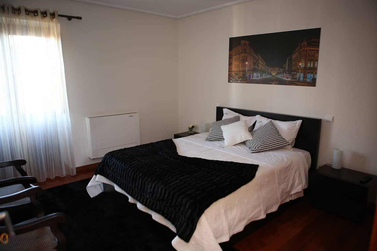 Quarto bem organizado com uma cama, uma cadeira, uma mesa de cabeceira e um quadro na parede.