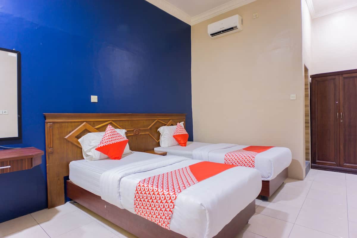 Quarto de hotel com duas camas, cabeceira de madeira, colcha com padrão vermelho e branco e uma parede azul decorativa.