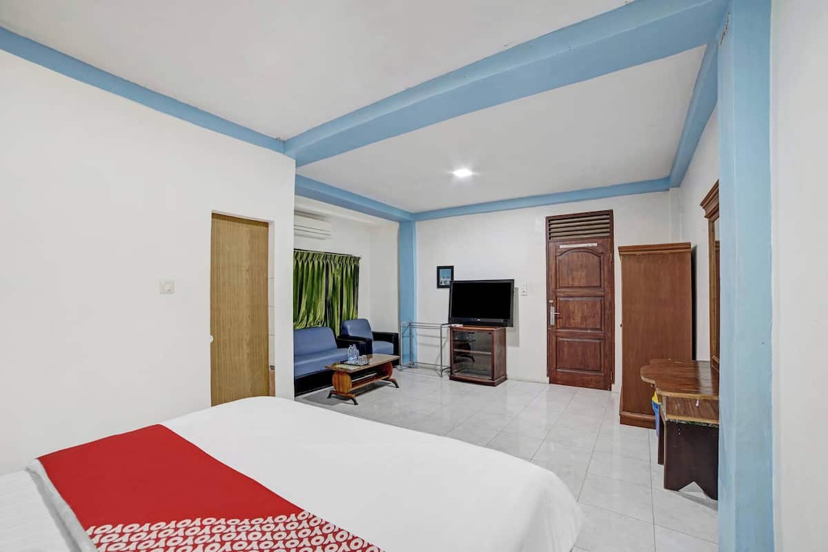 Quarto de hotel com cama, televisão, sofá, escrivaninha e porta.