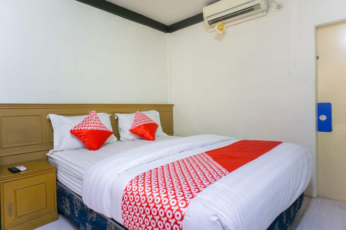 Cama bem arrumada com colcha estampada, dois travesseiros e mesa de cabeceira com controle remoto.