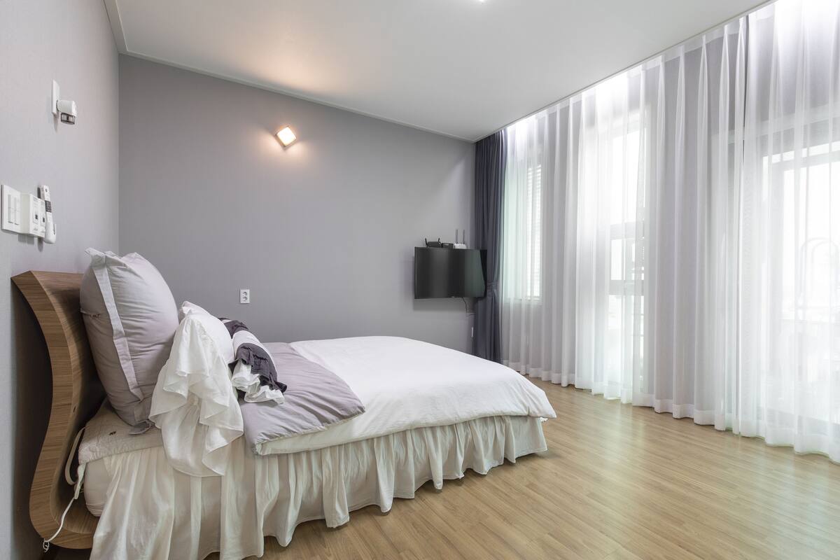 Um quarto moderno com cama, cortinas, televisão de tela plana e cabeceira de madeira.
