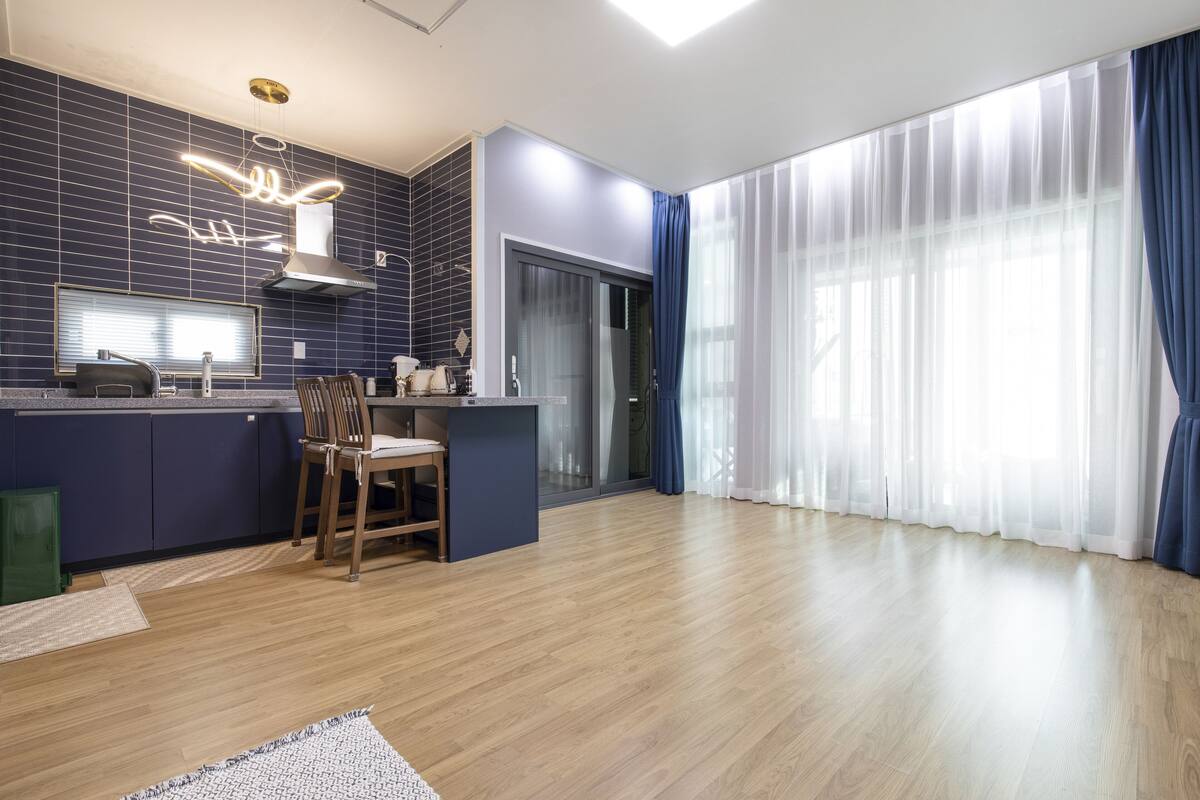 Cozinha moderna com ilha integrada, área de jantar com uma cadeira e uma janela grande com cortinas leves.