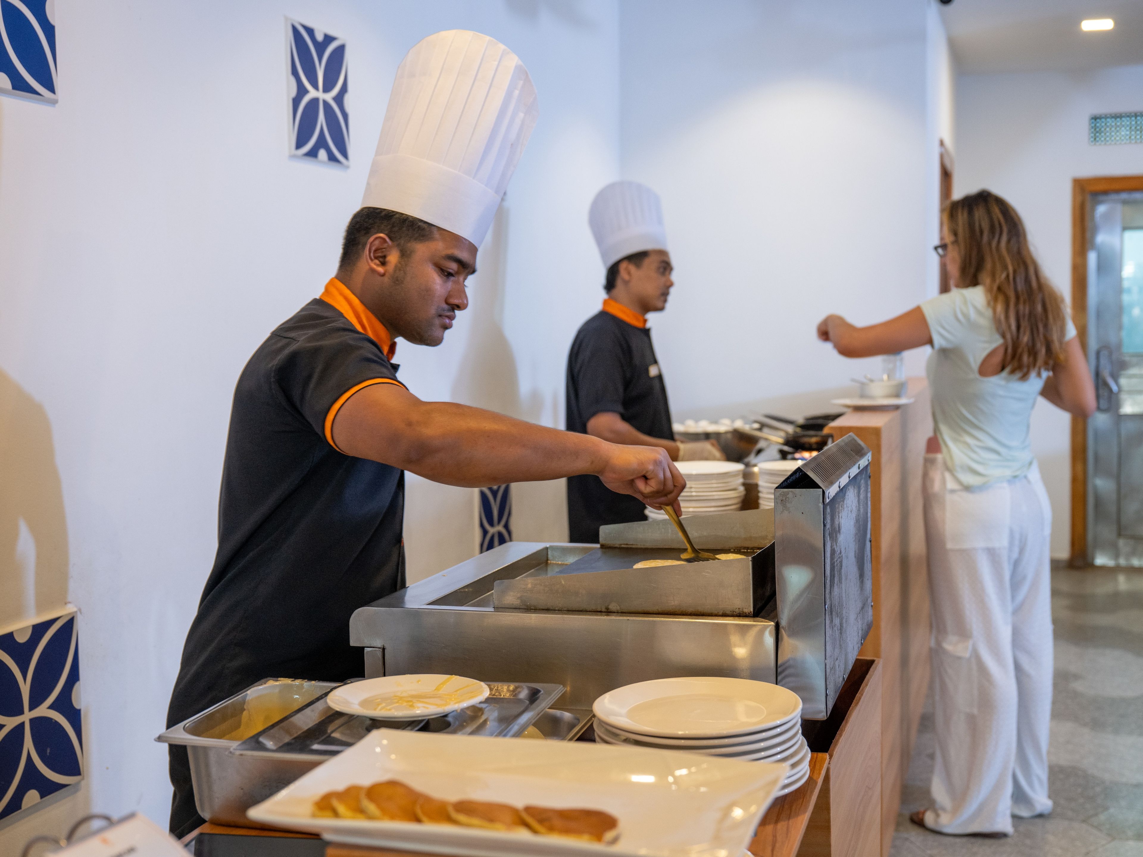 Disposição de buffet com funcionários servindo comida, mesa de buffet e balcão com pratos e tigelas.