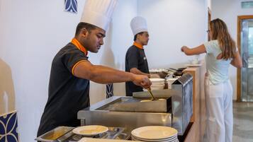 Disposição de buffet com funcionários servindo comida, mesa de buffet e balcão com pratos e tigelas.