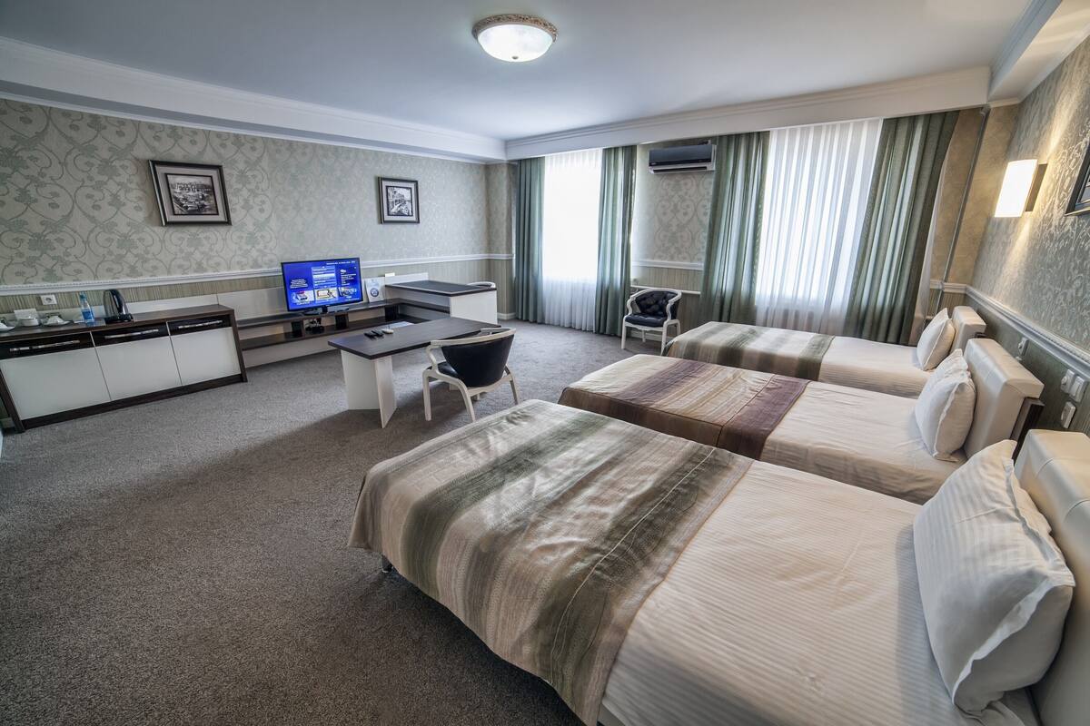 Quarto de hotel com duas camas, uma mesa, uma cadeira, uma televisão e um minibar.