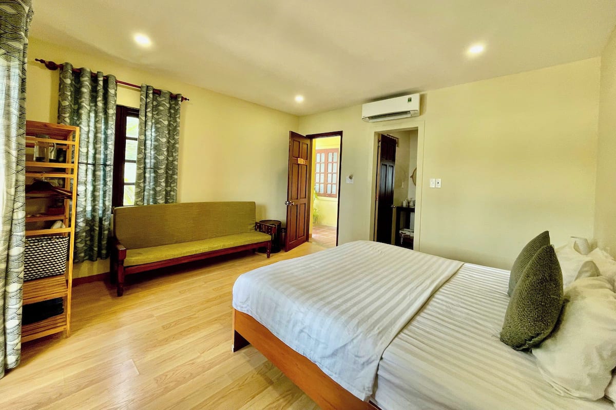 Quarto com cama, um banco de madeira, um guarda-roupa e uma estante com cortinas estampadas.