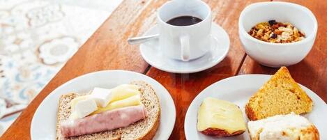Uma mesa de madeira com itens de café da manhã, incluindo torradas com queijo e presunto, uma xícara de café e uma tigela de cereal.