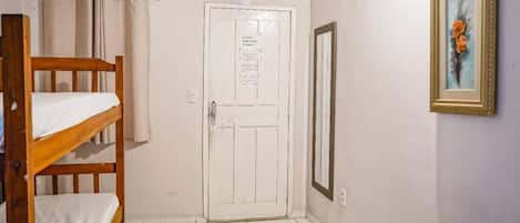 Um quarto com cama de solteira e beliche, uma porta com aviso, uma televisão e um quadro pendurado na parede.