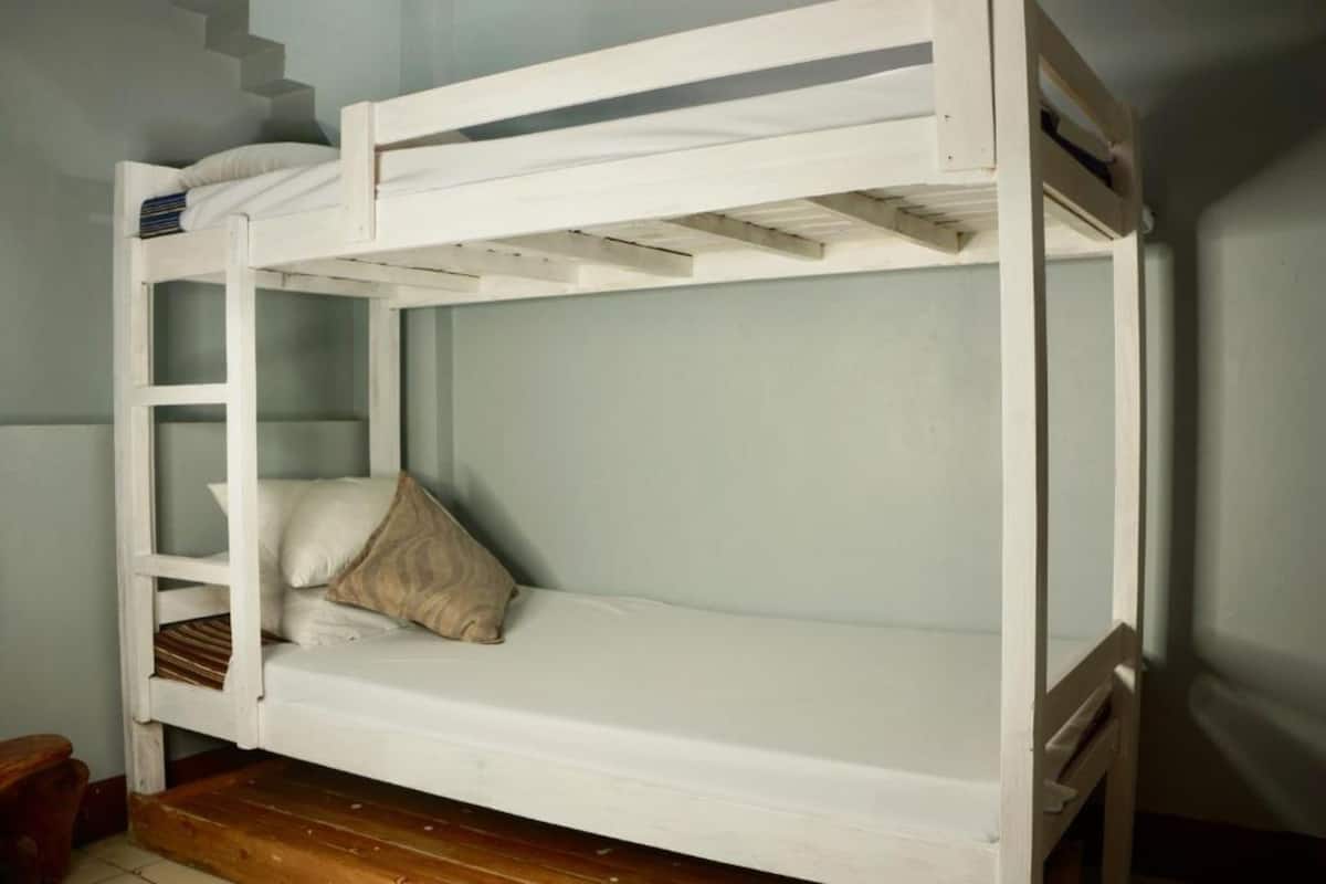 Uma cama beliche com escada de madeira, um travesseiro e um banquinho pequeno de madeira.