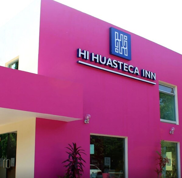 Um edifício com fachada rosa vibrante e uma placa que diz 'HI HUASTECA INN'.
