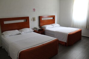 Duas camas de solteiro com cabeceiras de madeira, roupa de cama branca e um aviso de proibido fumar na parede.