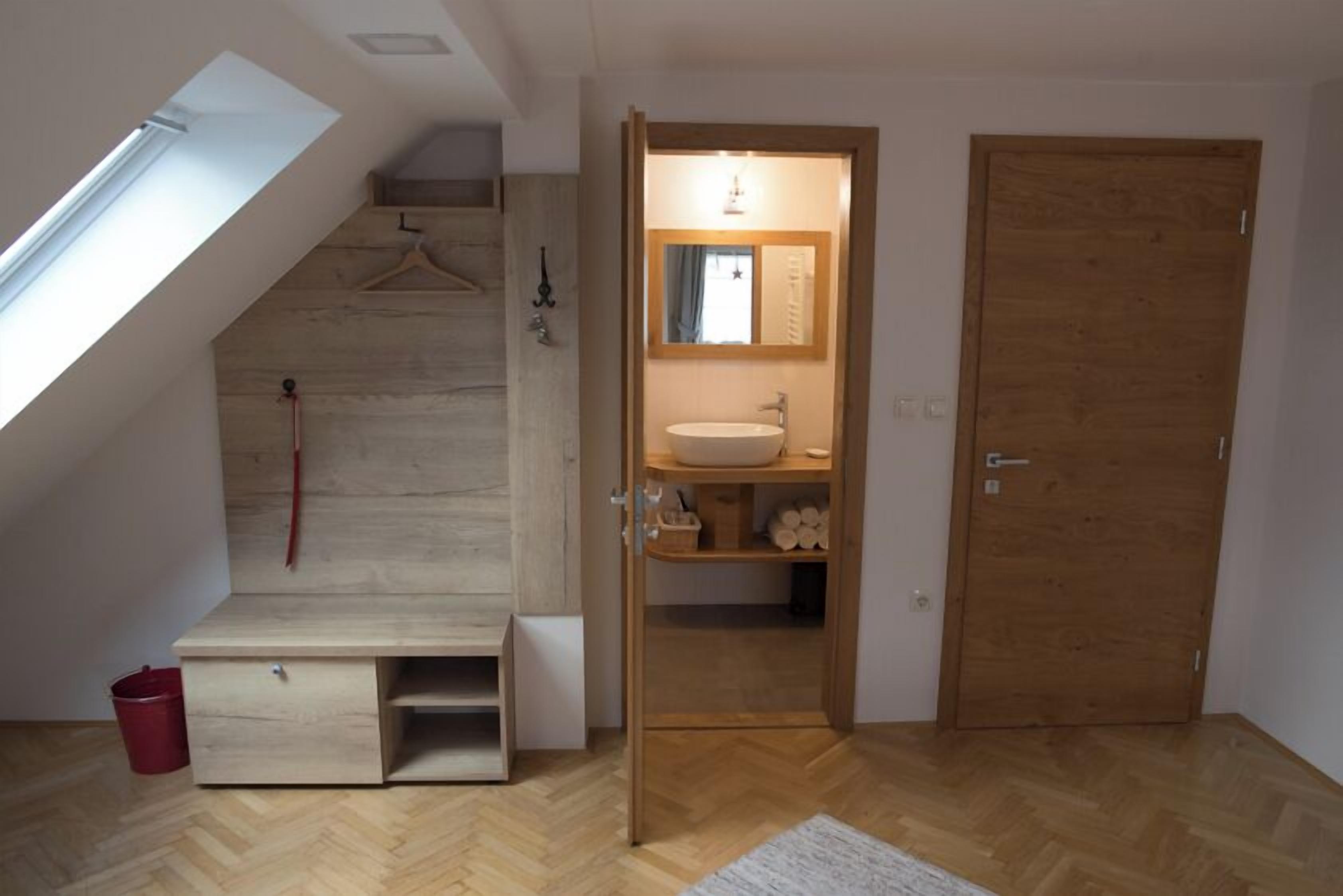 Um quarto com um banco de madeira, uma pia pequena, um espelho e uma porta.