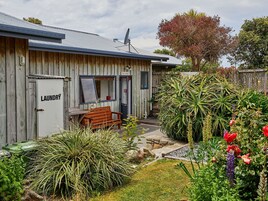 Um edifício rústico com lavanderia, um banco e um jardim com diversas plantas e flores.