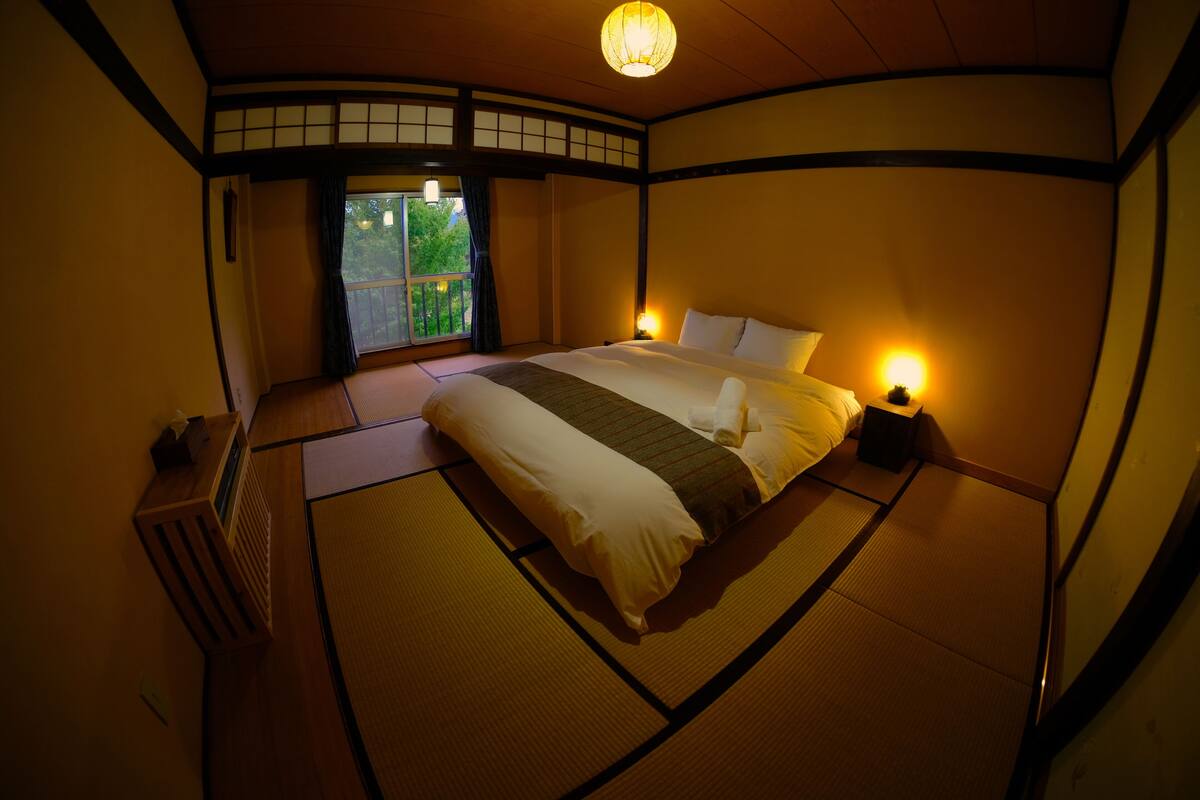 Quarto tradicional japonês com tatame, cama baixa e porta deslizante para uma varanda.