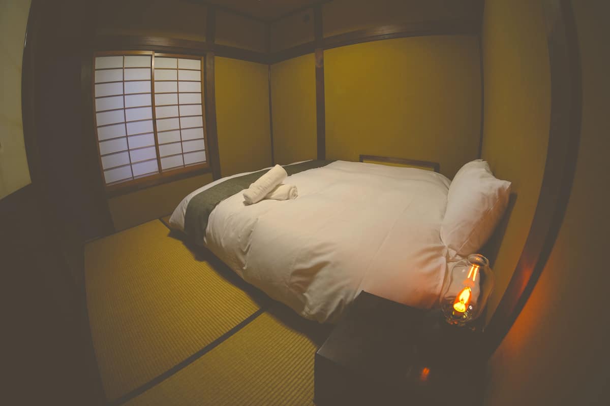 Um quarto tradicional japonês com tatame, futon, janela com tela shoji e luminária de cabeceira.