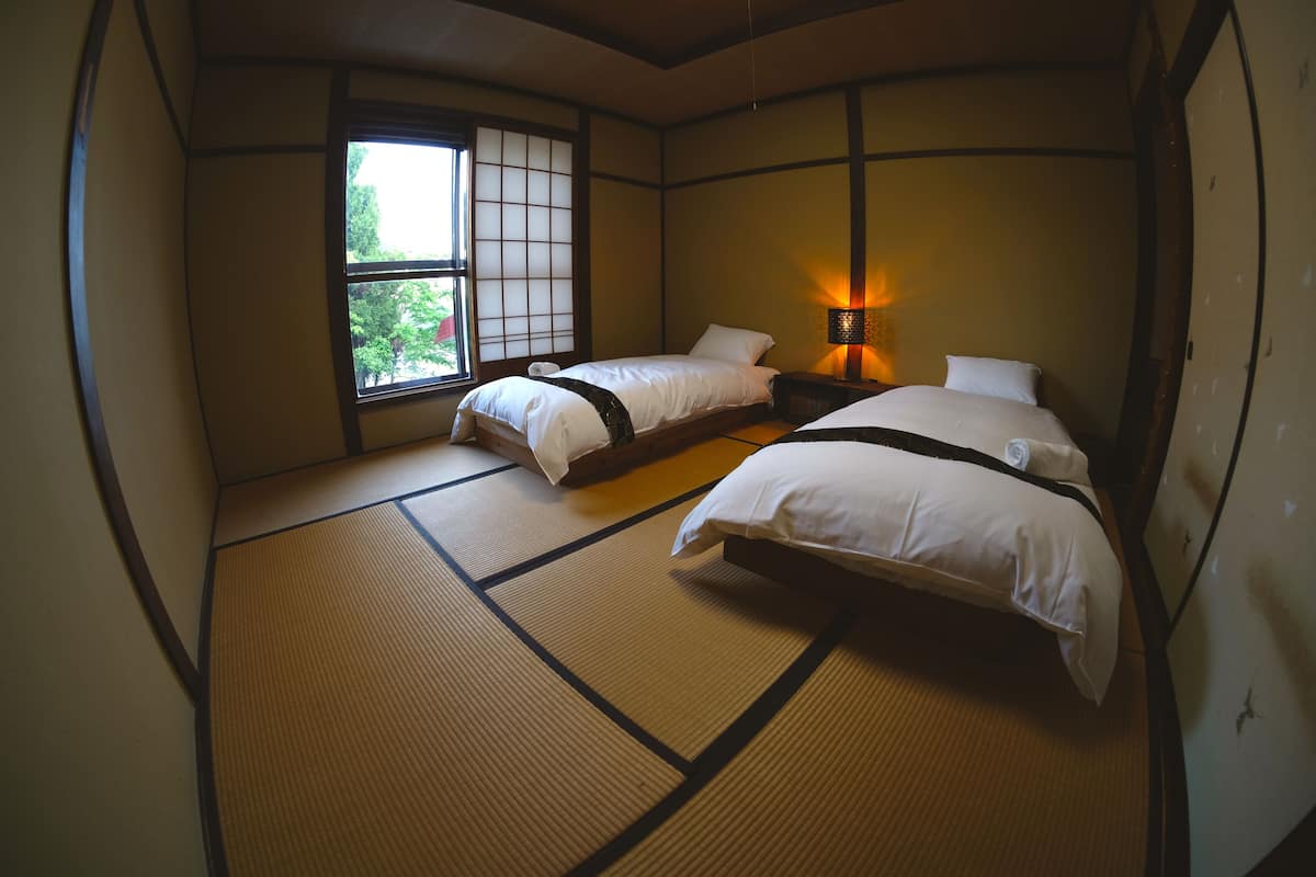 Quarto japonês tradicional com tatames, duas camas, uma janela com biombos shoji e um abajur.