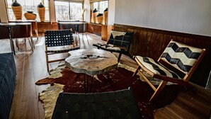 Uma sala de estar ampla com piso de madeira, um tapete grande e diversas opções de assento, incluindo um sofá e poltronas.