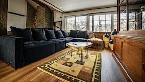 Uma sala de estar moderna com um sofá escuro, uma mesa de centro redonda e uma janela grande com vista para o exterior.