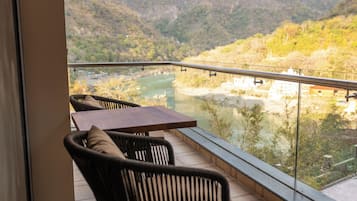 Varanda com vista para um rio e montanhas. Há duas cadeiras e uma mesa.