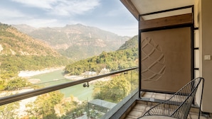 Uma varanda com vista para um rio e montanhas, uma mesa com cadeiras e uma porta decorativa.
