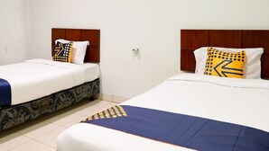Duas camas de solteiro com cabeceiras de madeira, roupa de cama branca e almofadas decorativas com padrões geométricos.