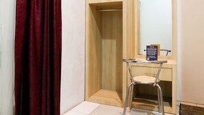 Quarto pequeno com guarda-roupa de madeira, espelho, cadeira e cortina vermelha.