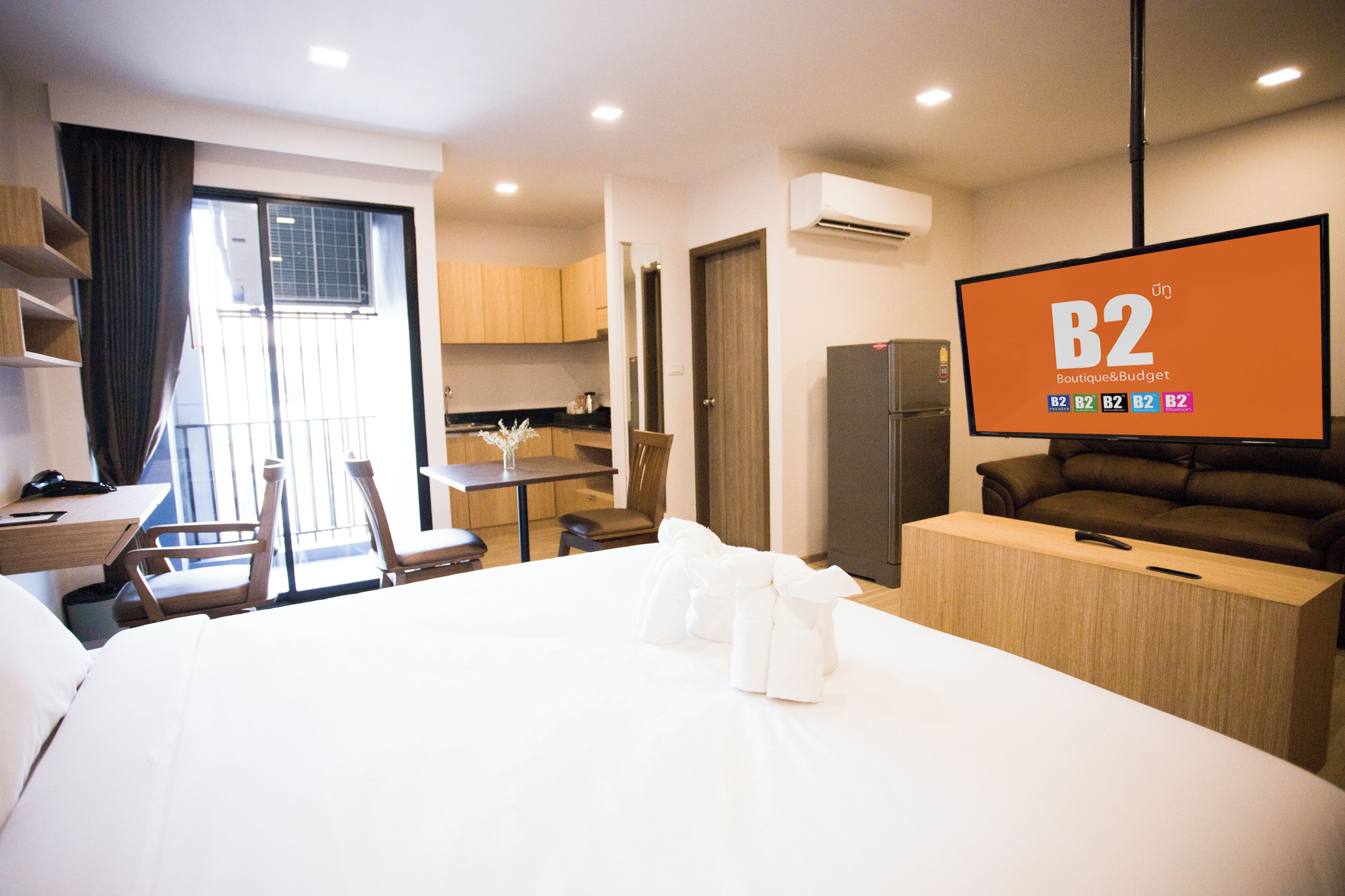 Quarto de hotel com cama grande, escrivaninha, poltrona, sofá, televisão e varanda com vista.