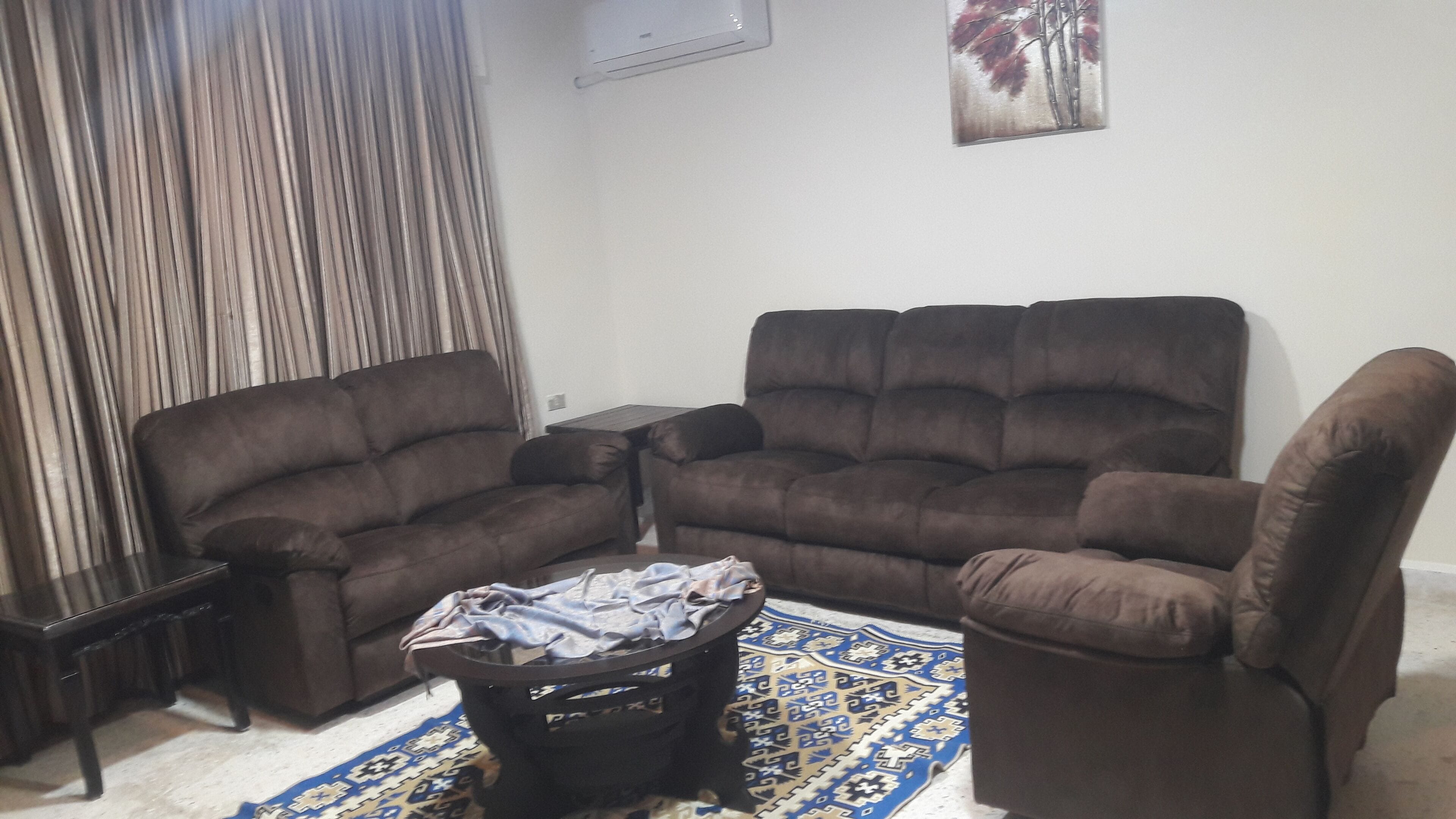 Uma sala de estar com dois sofás marrons, uma mesinha e um tapete estampado.
