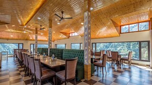 Um restaurante com chão quadriculado, teto de madeira e grandes janelas com vista para a floresta.