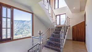 Uma escadaria moderna com guarda-corpos de metal e vista para uma paisagem montanhosa através de grandes janelas.